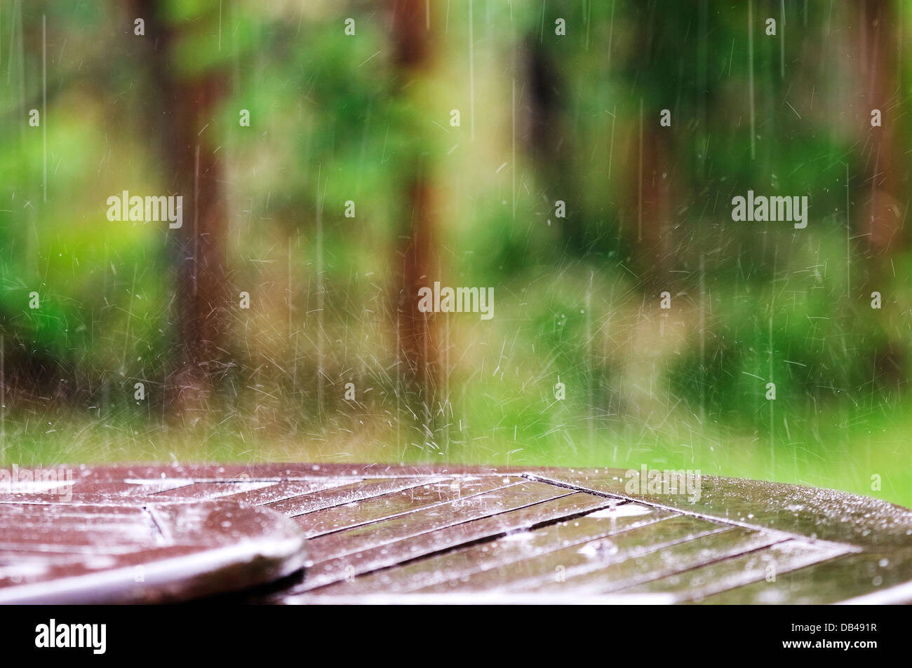 Raindrops dramatically splashing on a wooden garden table during a ...