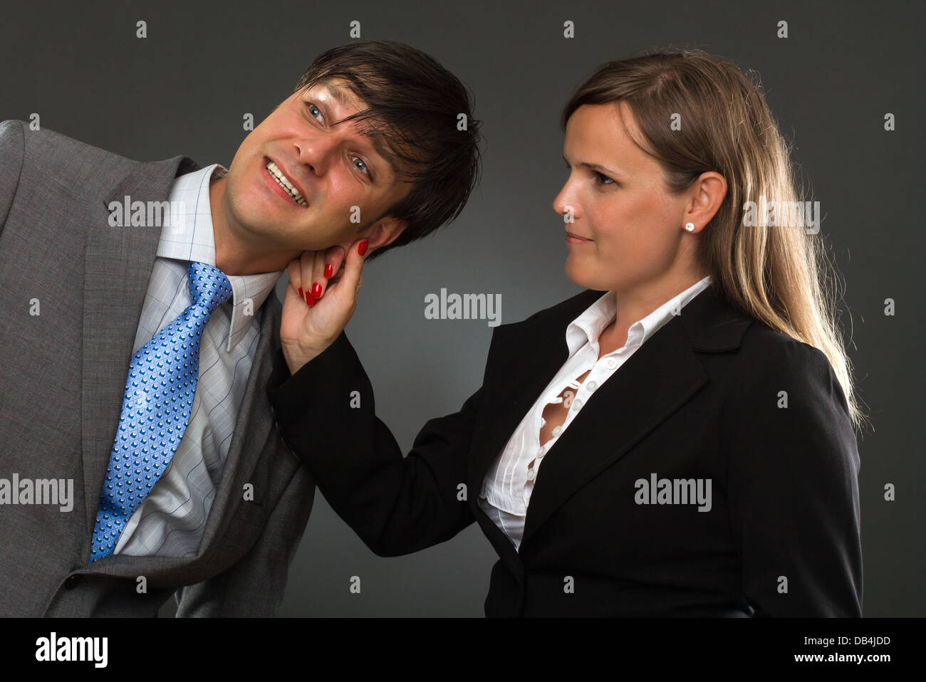 a hand pulling a businessman ear on gray Stock Photo - Alamy