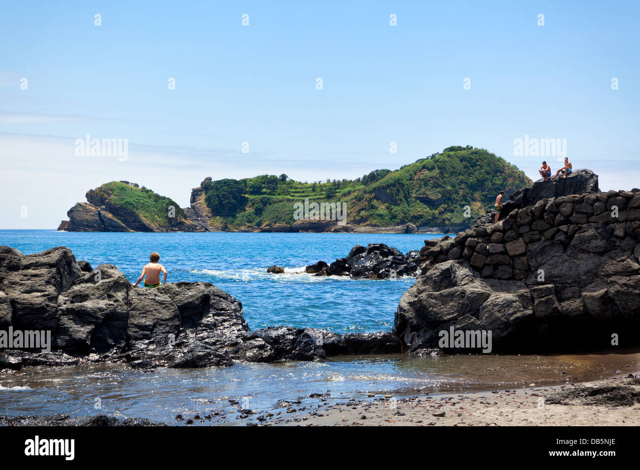 Boys playing on the rocks opposite to the islet of Vila Franca off São ...