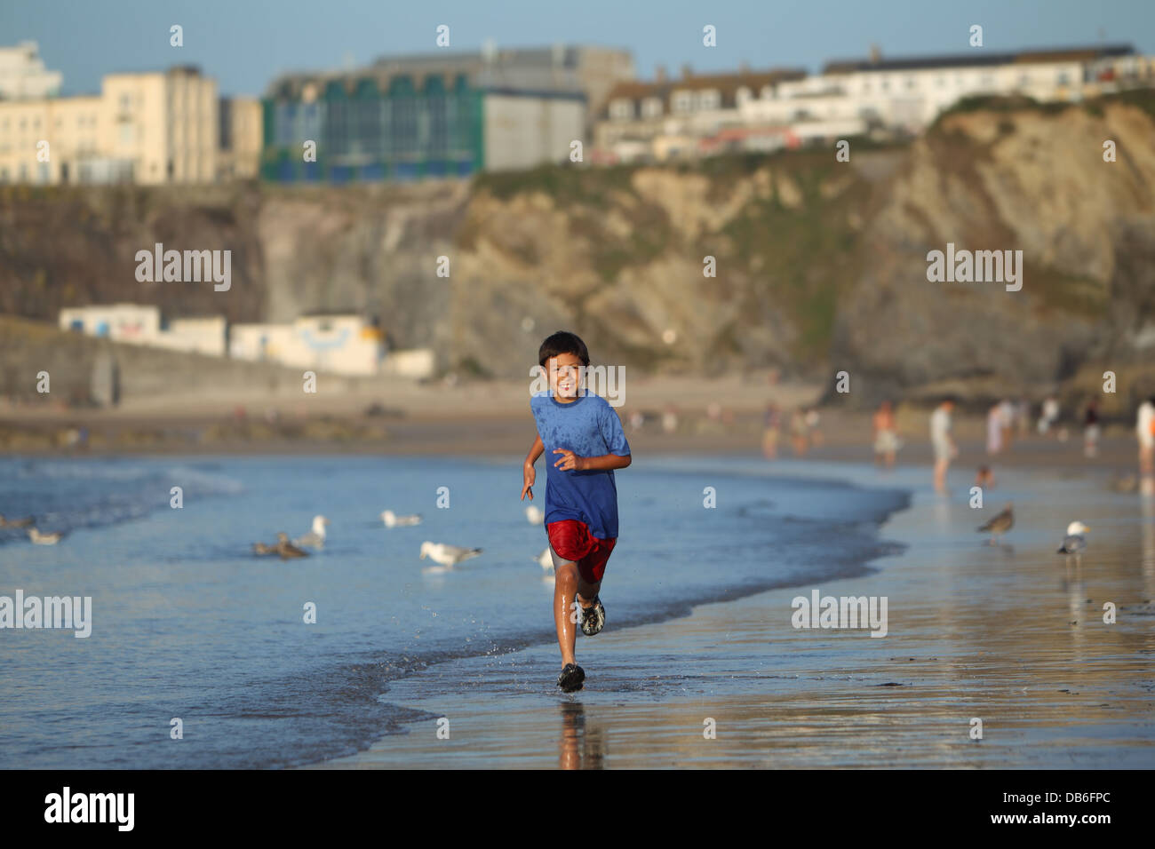 Young boy plays and runs in the surf along an English beach near sunset ...
