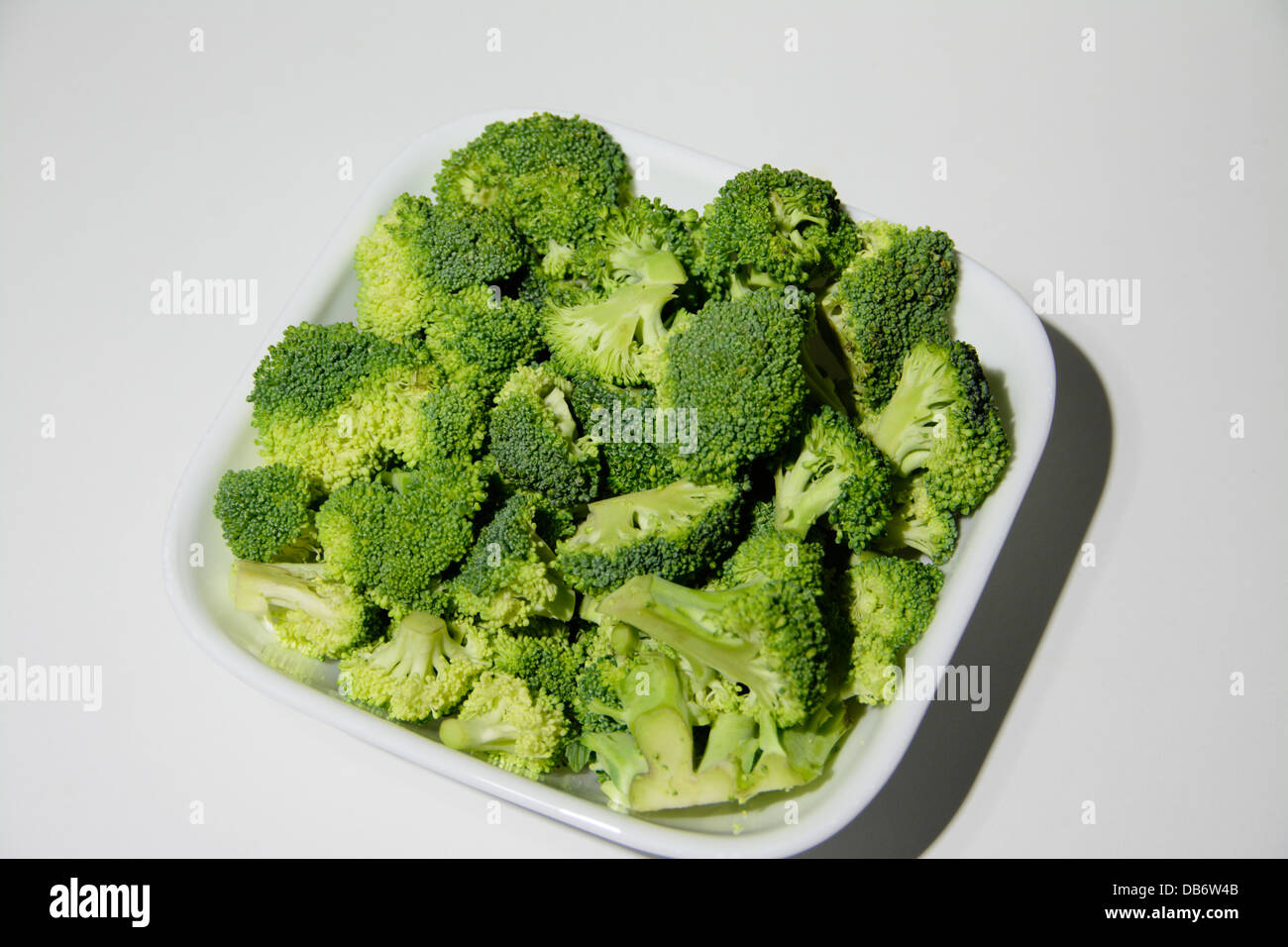 A white plate containing cut up broccoli crowns on a white background ...