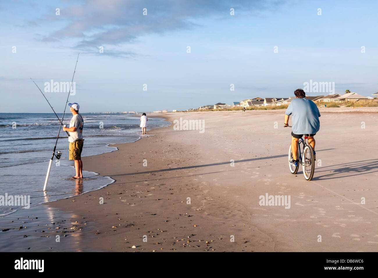 Man riding bicycle while sea angler with fishing rod / pole on beach ...