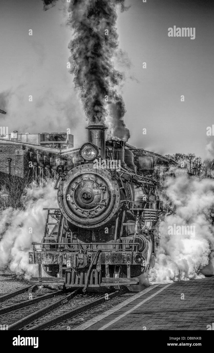 A steam-powered locomotive sits at a siding, emitting smoke while ...