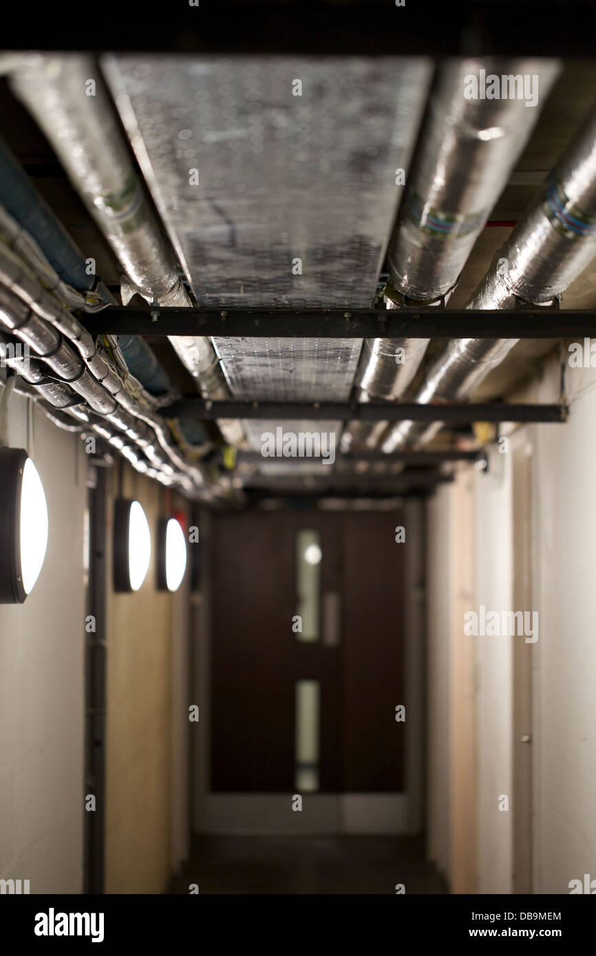 An underground basement passage way, dimly lit with pipes and services ...