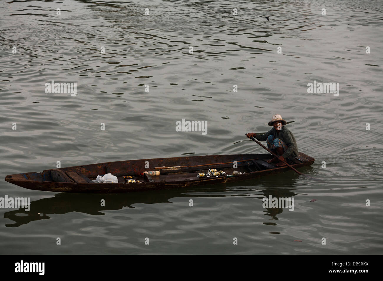 A native woman paddles a long flat boat carrying garbage in fishing ...