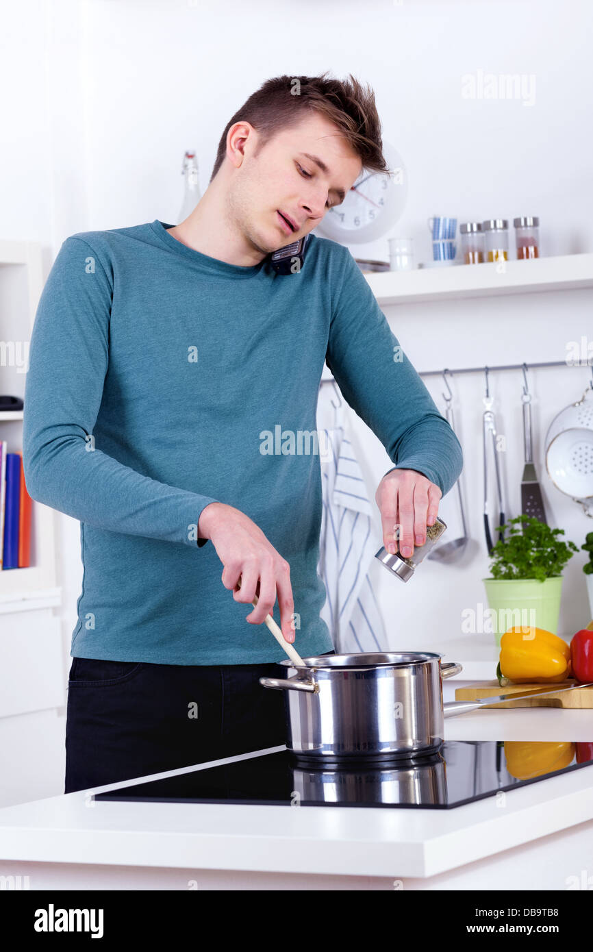 young man cooking a meal and talking on the phone in his kitchen Stock ...