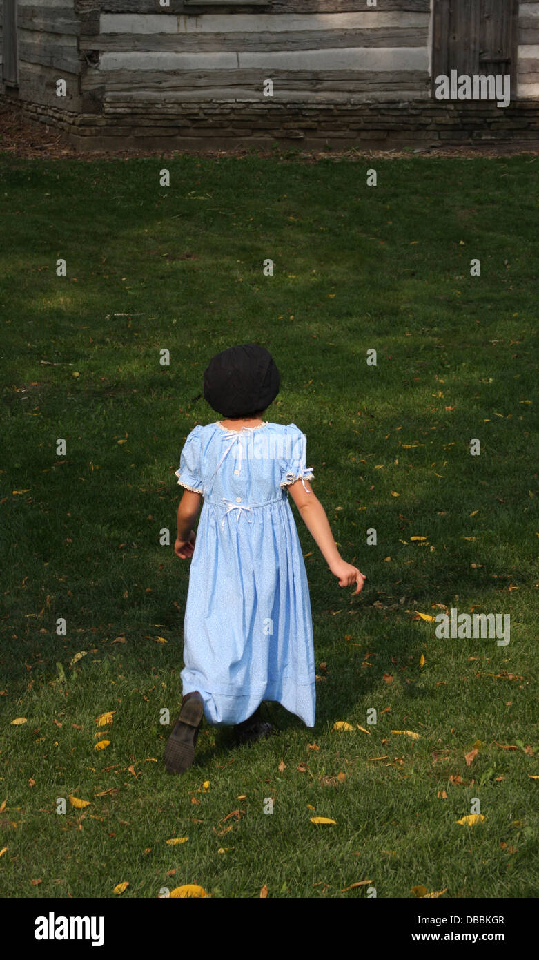 A young child in a prairie dress walking to a log cabin Stock Photo - Alamy