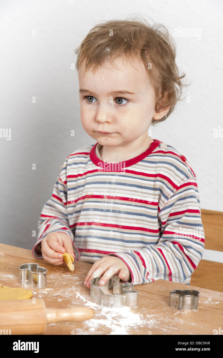 vertical image of 2 year old child making biscuit at wooden desk Stock ...