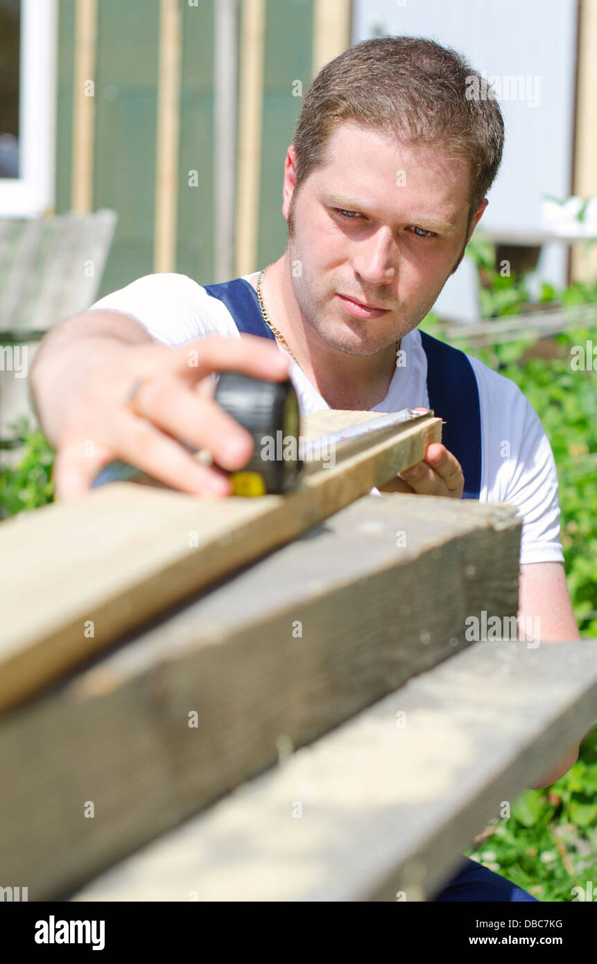Handsome handyman measuring wooden plank outdoors Stock Photo - Alamy