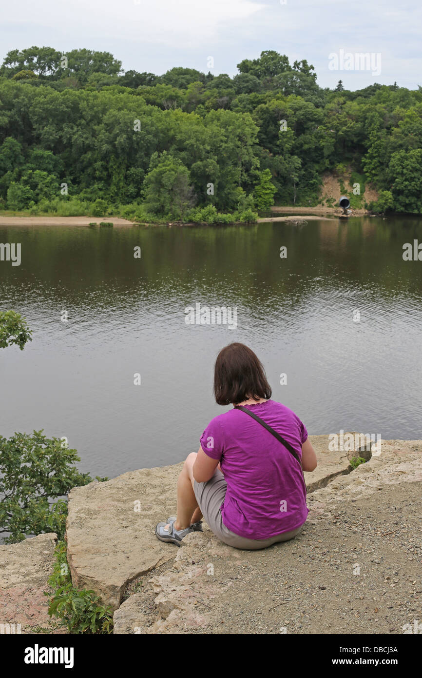 A woman sitting on a rock overlook above the Mississippi River in St ...