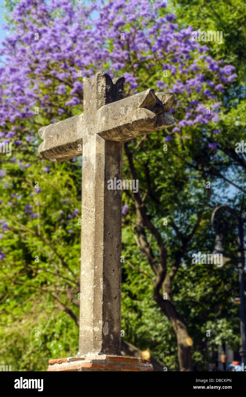 A stone cross in Mexico City with purple flowers and trees in the ...