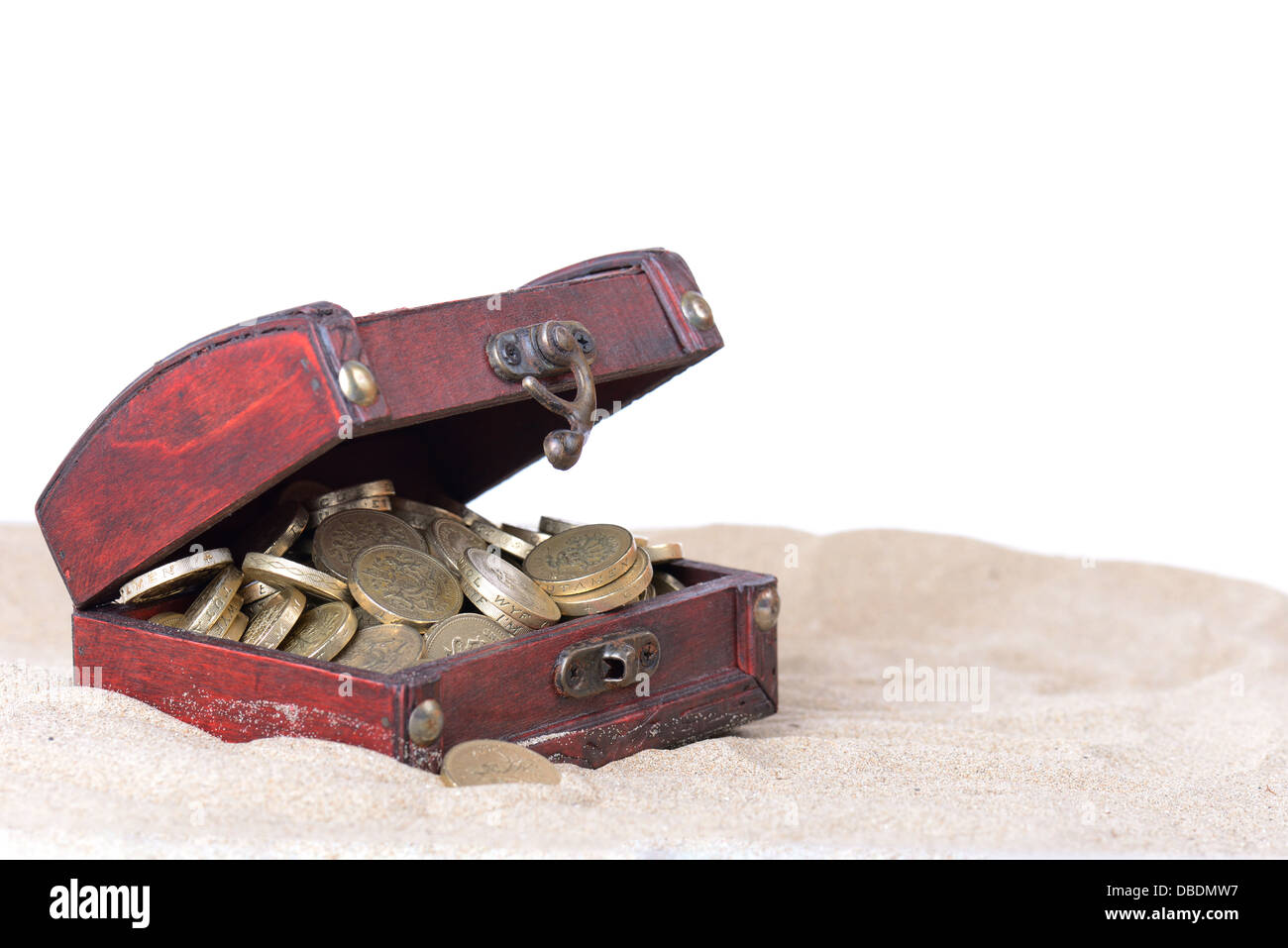 small treasure box open with gold coins inside part buried in the sand ...