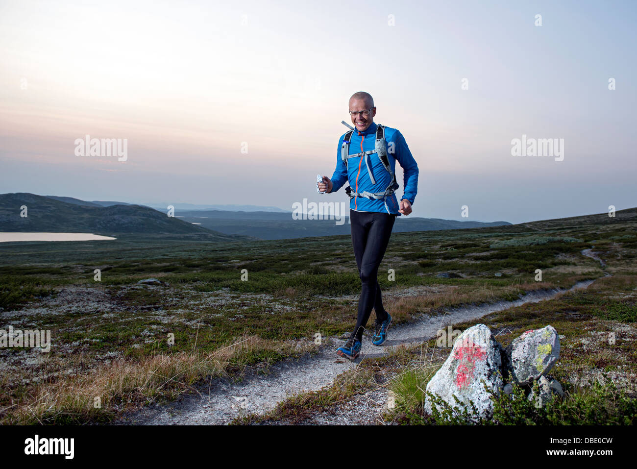An athlete running on the Hardangervidda Plateau, Norway as night falls ...