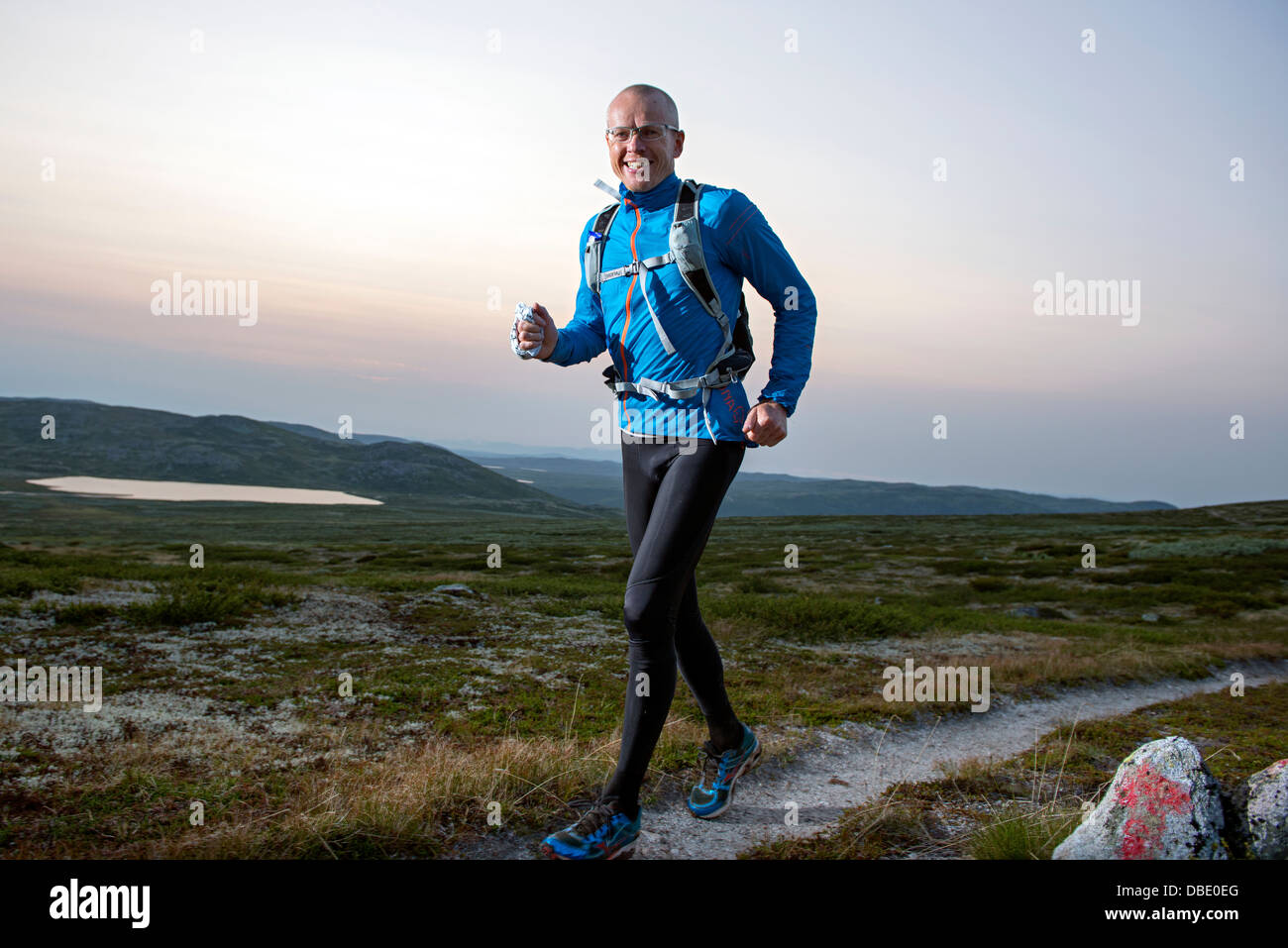 An athlete running on the Hardangervidda Plateau, Norway as night falls ...