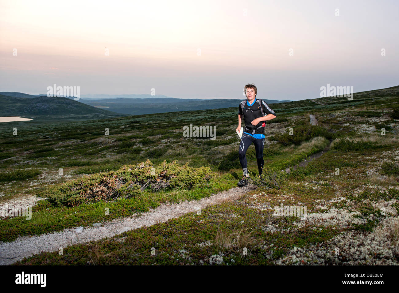 An athlete running on the Hardangervidda Plateau, Norway as night falls ...