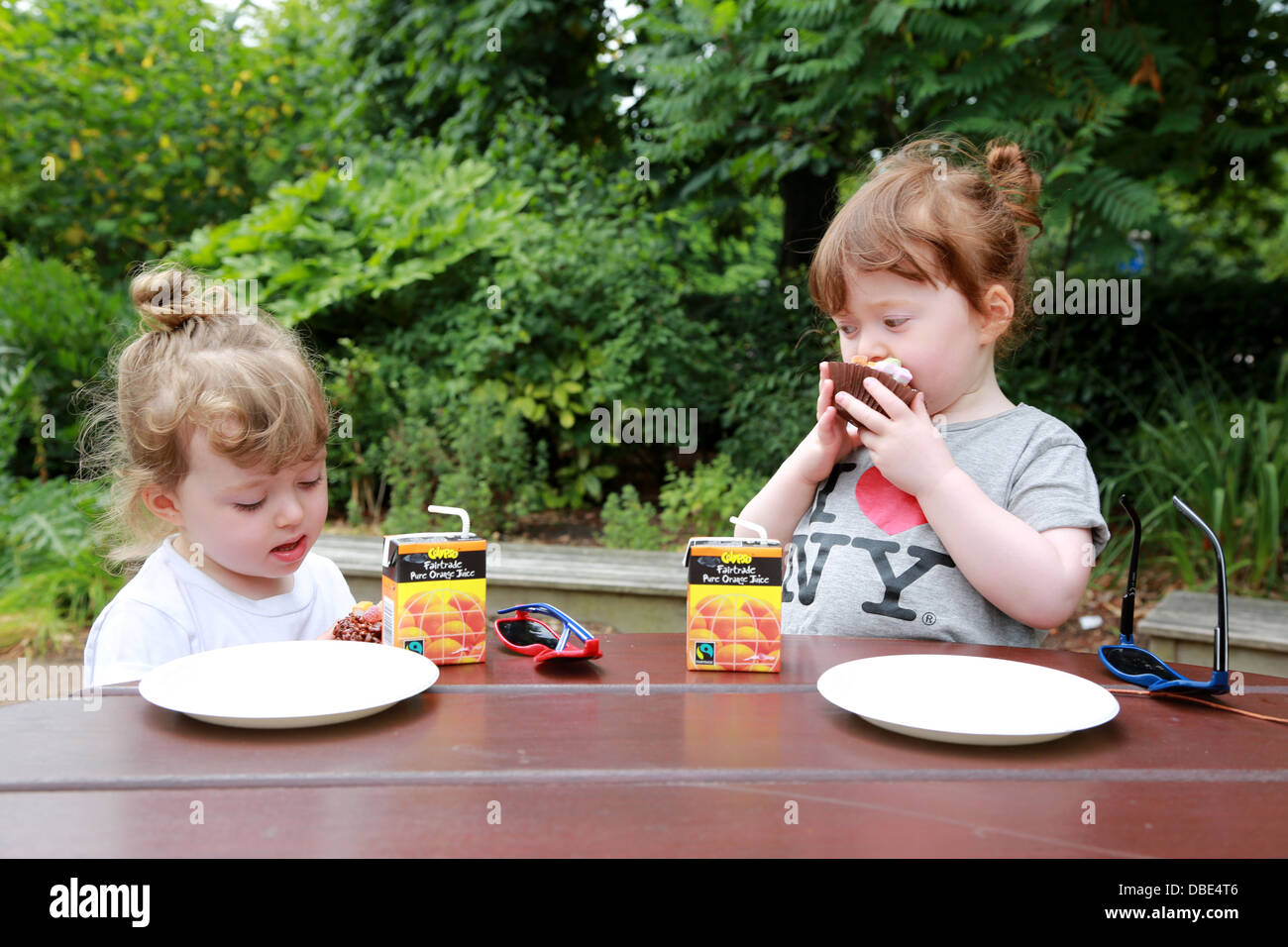 Twin girls having a snack in the park Stock Photo - Alamy