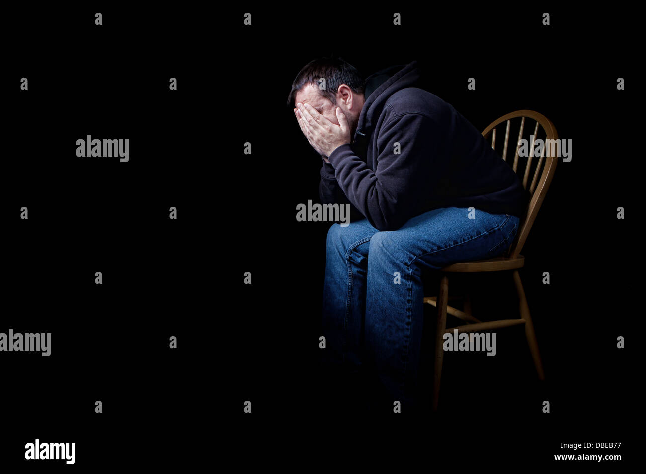 A depressed man sitting in a chair with his hands over his face, shot ...