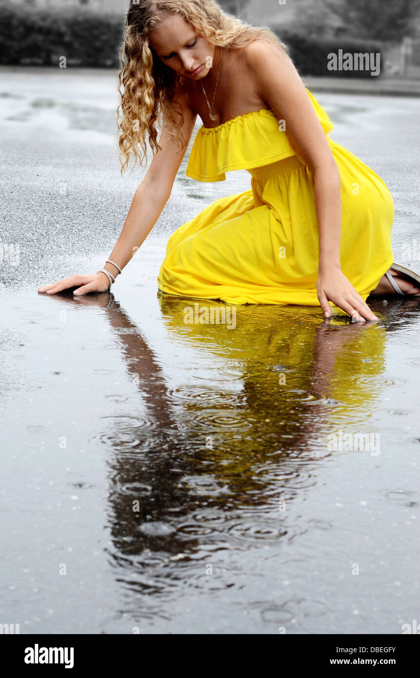 A young woman looks at her reflection in a yellow dress in the rain ...