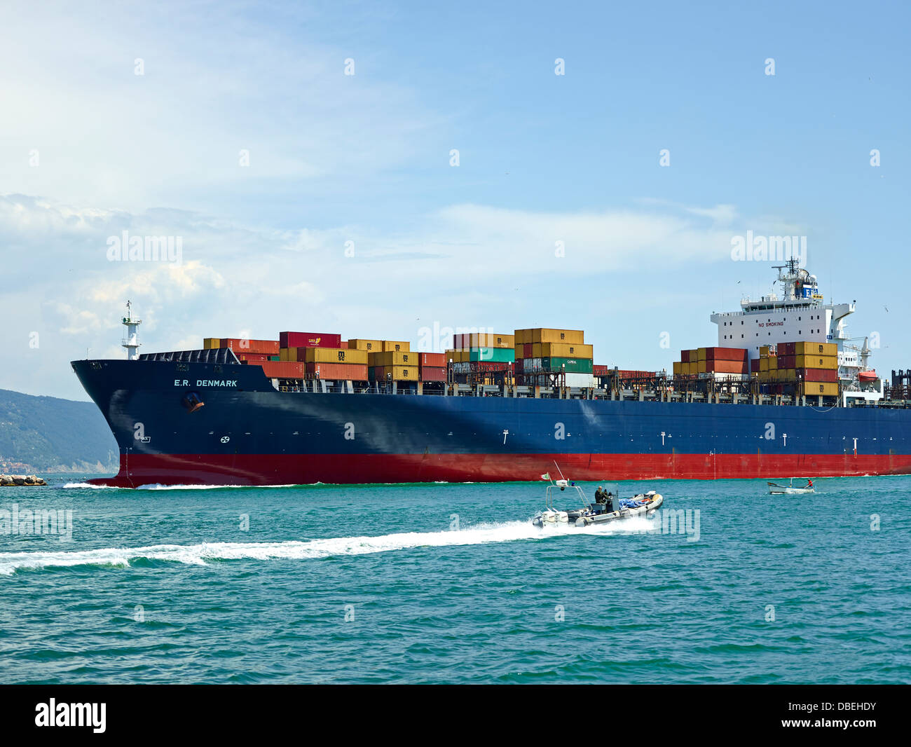 A small motorboat raft next to a large container ship sailing in the ...