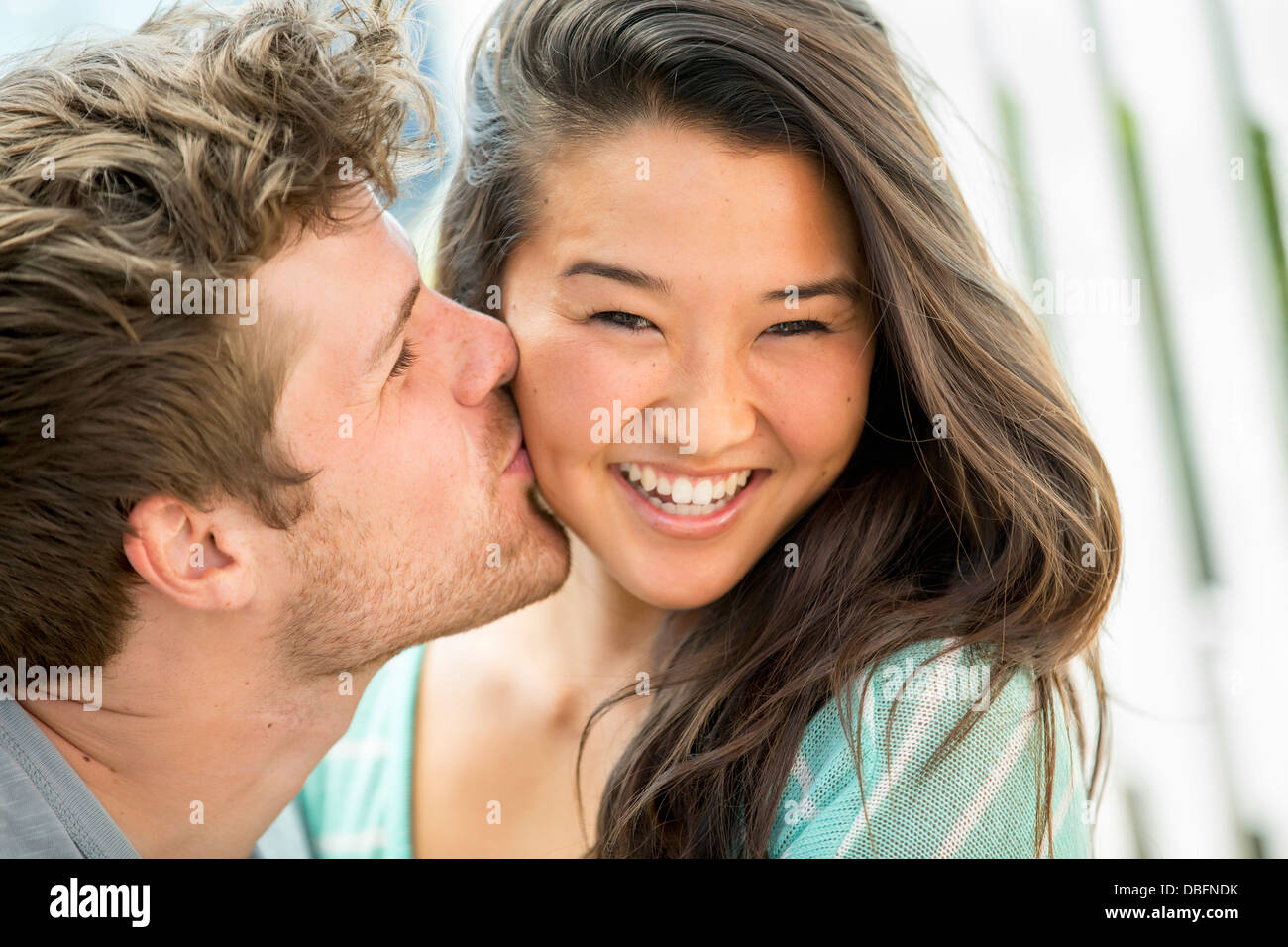 Man kissing girlfriend's cheek outdoors Stock Photo - Alamy