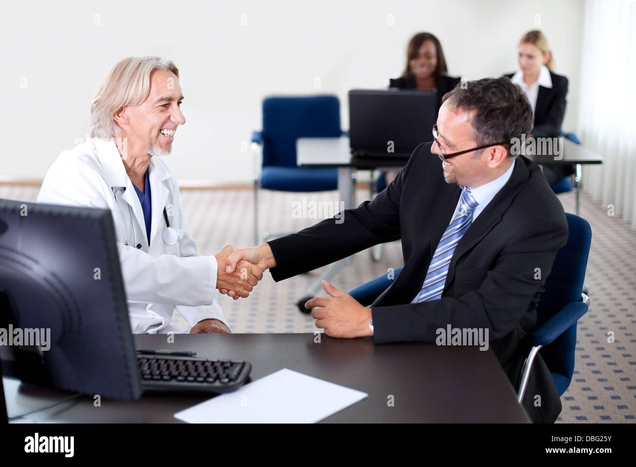 Doctor shaking hands with a patient at a desk Stock Photo - Alamy