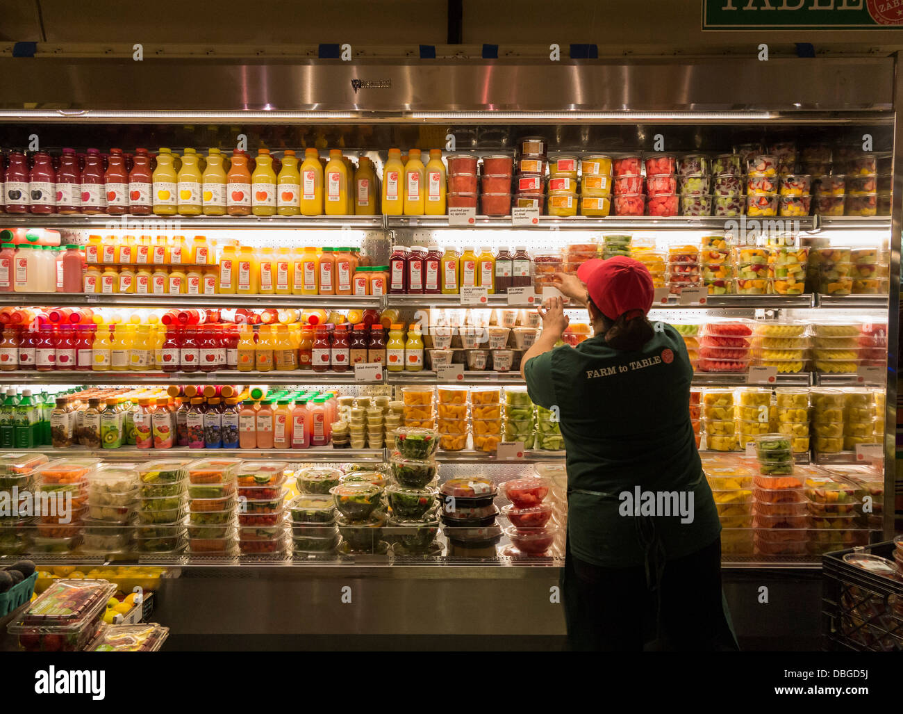 Woman worker stacking shelves in a fruit, salad and juice display in a ...
