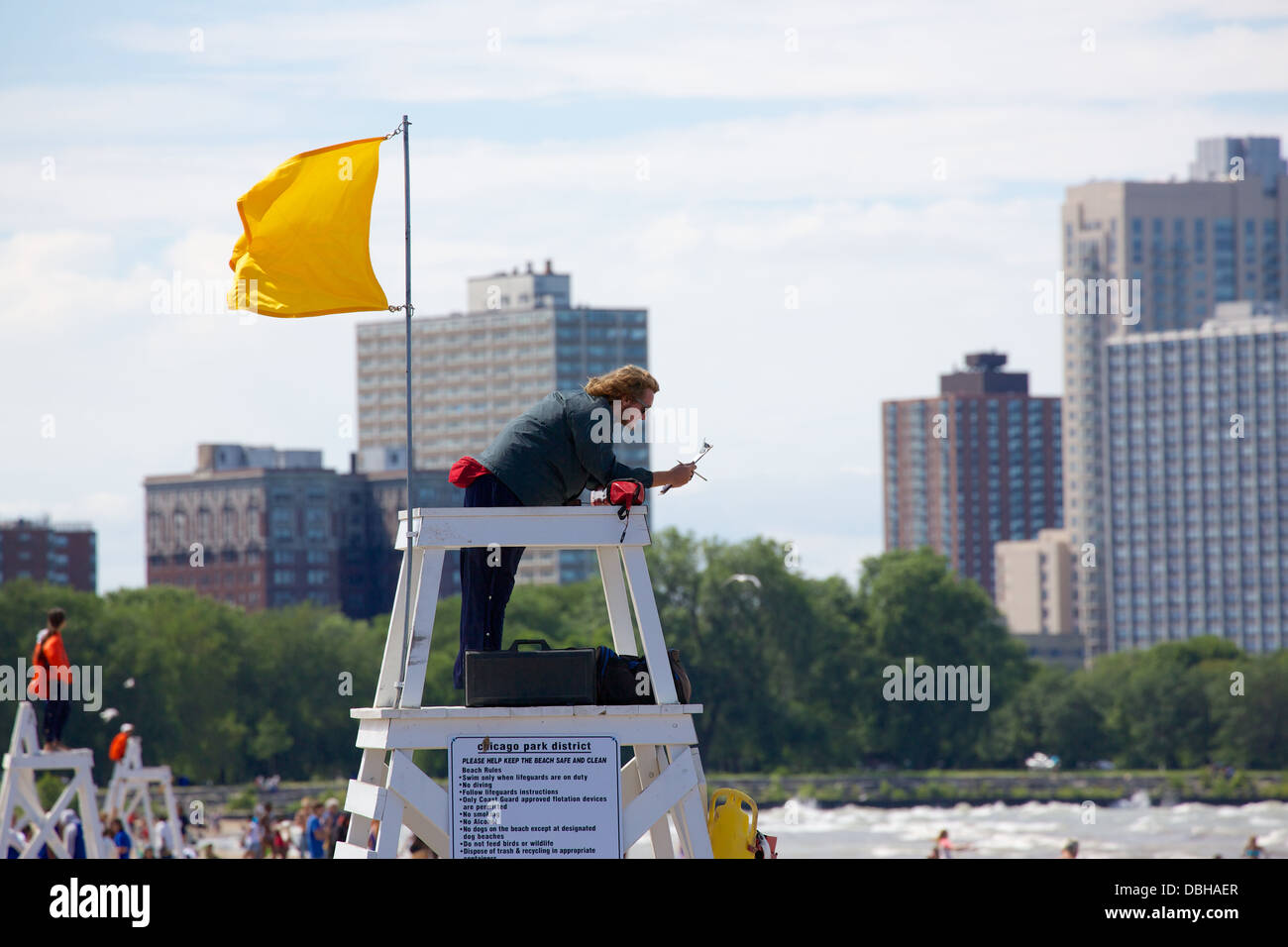 Lifeguard on guard tower with clipboard. Yellow flag warning hazardous ...