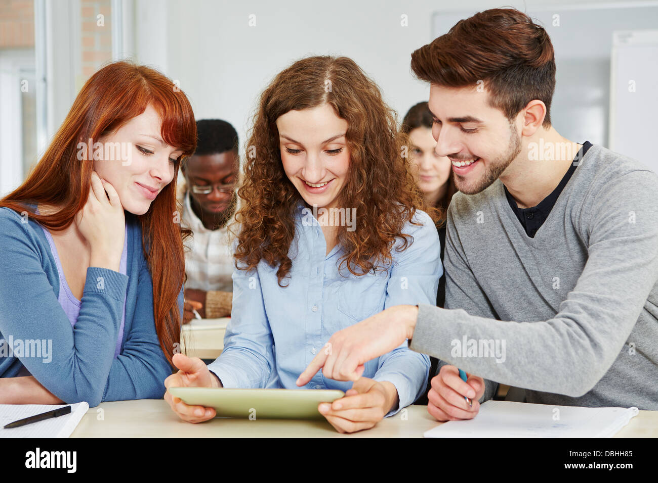 Three happy students learning in class with a tablet PC in classroom ...