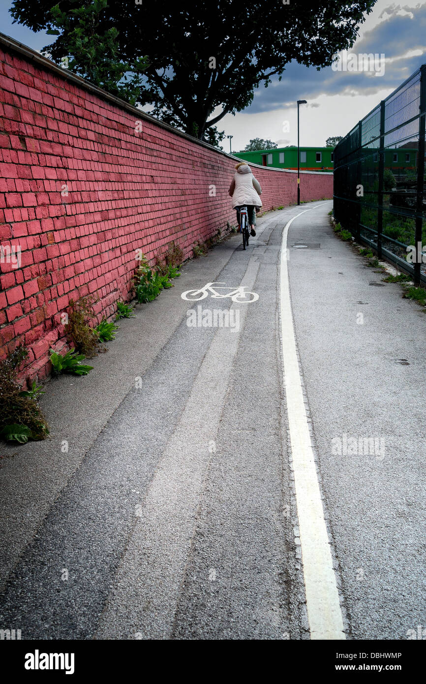A female cyclist on an urban cycle path at dusk, flanked by a wall and ...