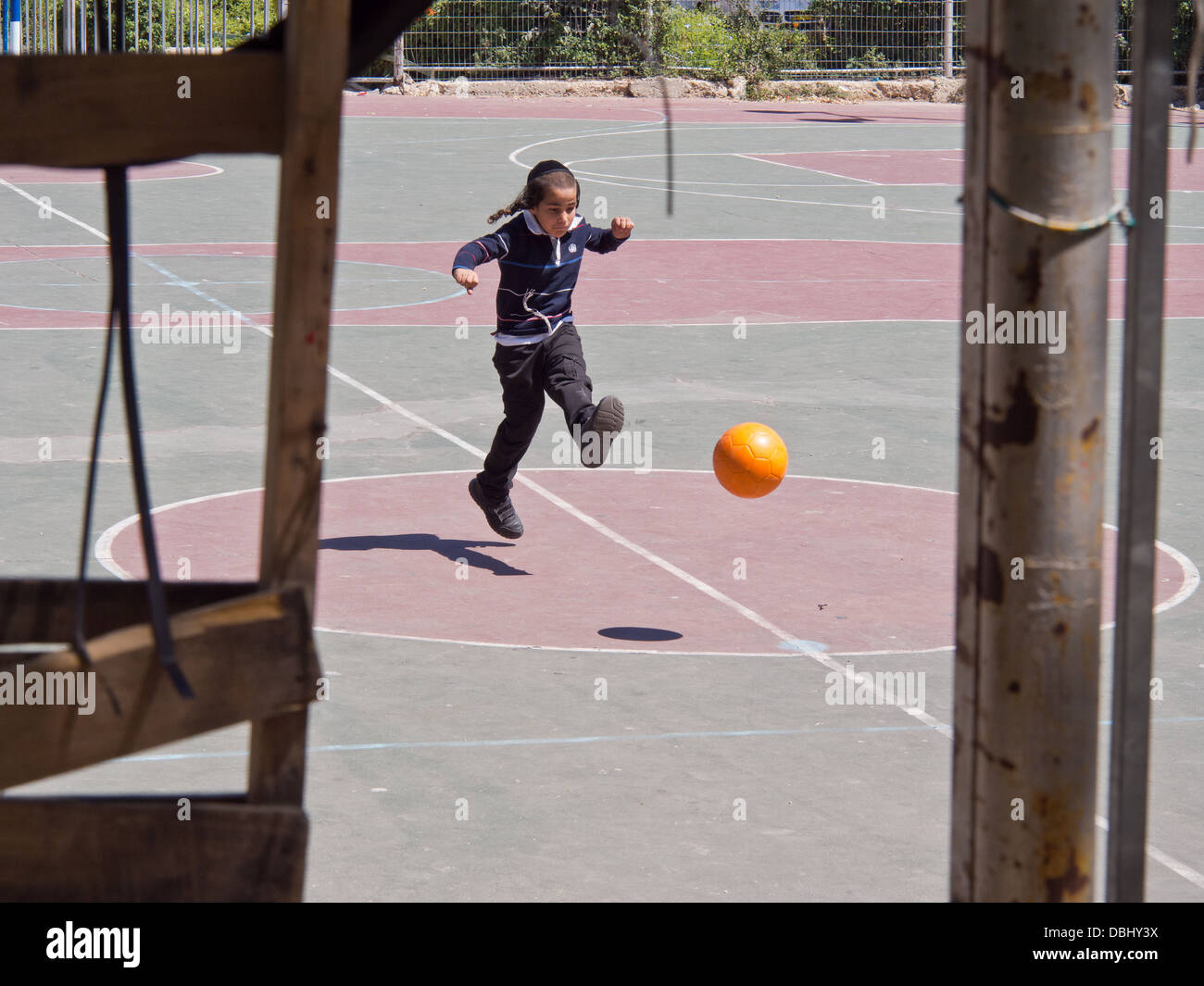 Orthodox religious Jewish boy with sidelocks kicks an orange ball in a ...
