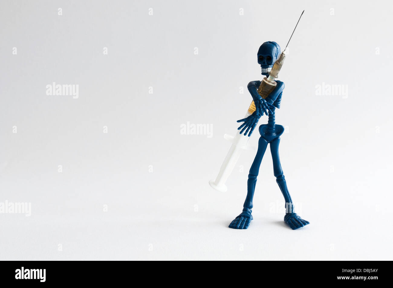 Blue rubber skeleton standing with syringe filled with transparent ...