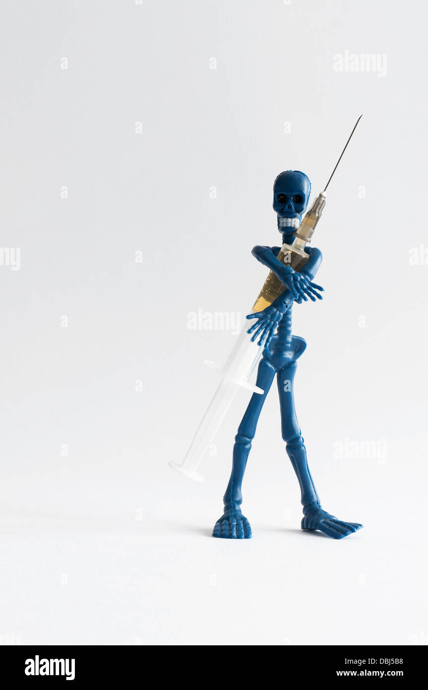 Blue rubber skeleton standing with syringe filled with transparent ...