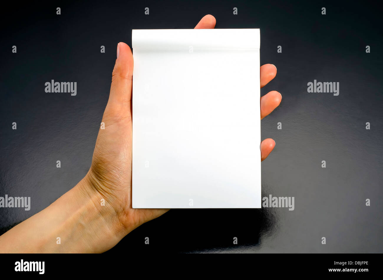 Female hands holding a blank white notebook. On a black background ...
