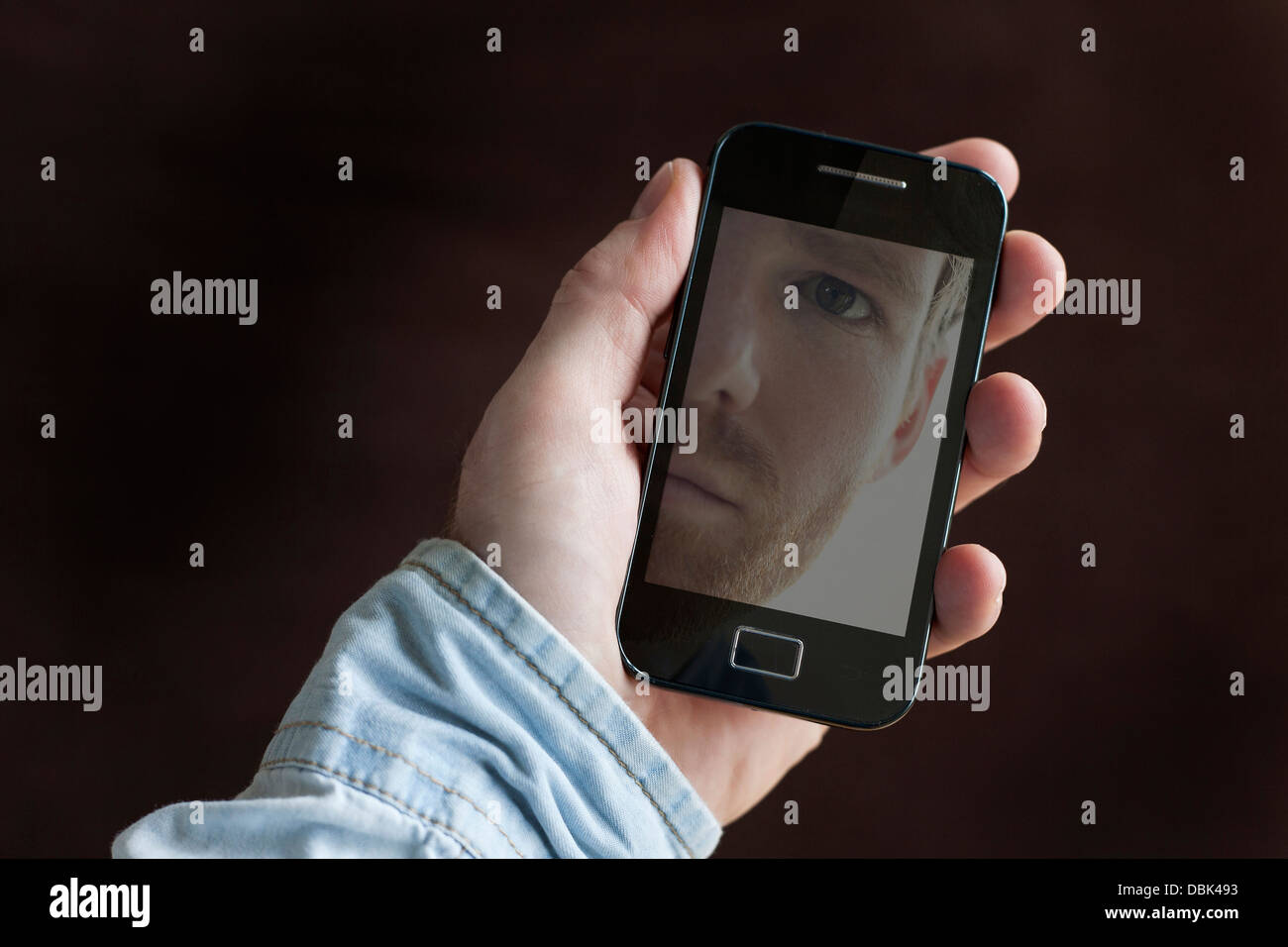 Man holding a mobile phone, reflection of his face on the screen ...