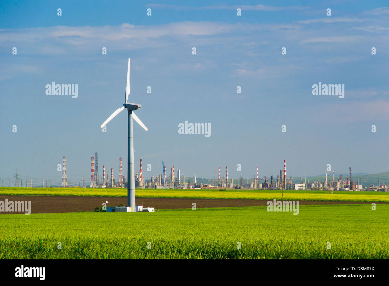 Wind turbine in a field of wheat and the chimneys of a petrol refinery ...