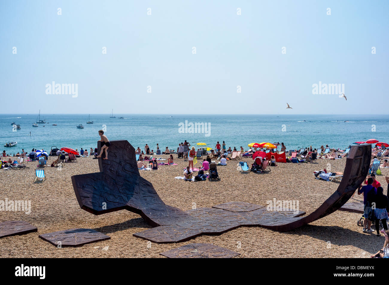 A young boy atop a work of art on Brighton Beach on a hot sunny ...