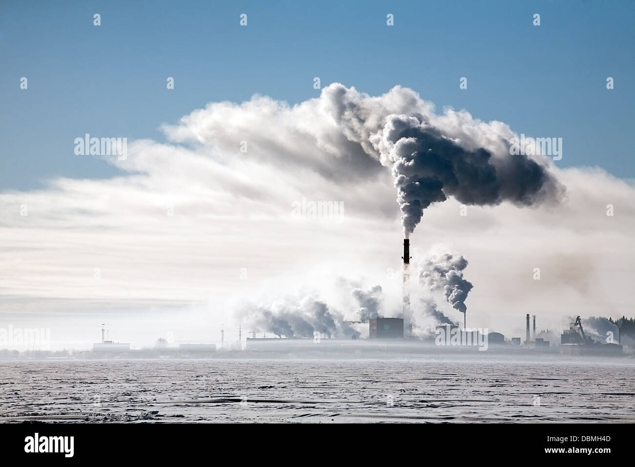 view of big factory with black smoke from its pipe on winter lake coast ...