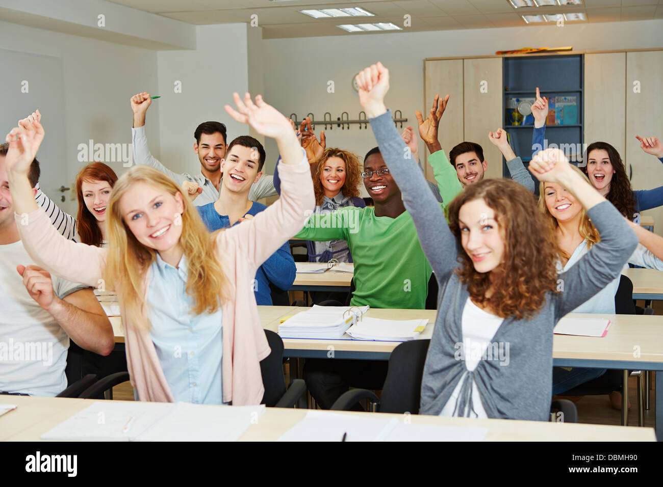 Many cheering students with hands raised in university class Stock ...