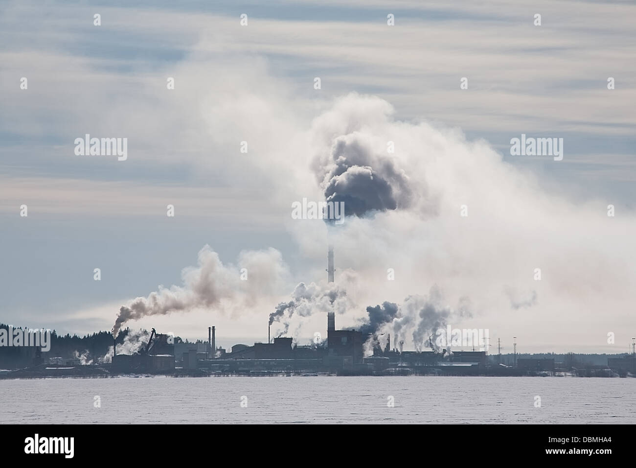 view of big factory with black smoke from its pipe on winter lake coast ...