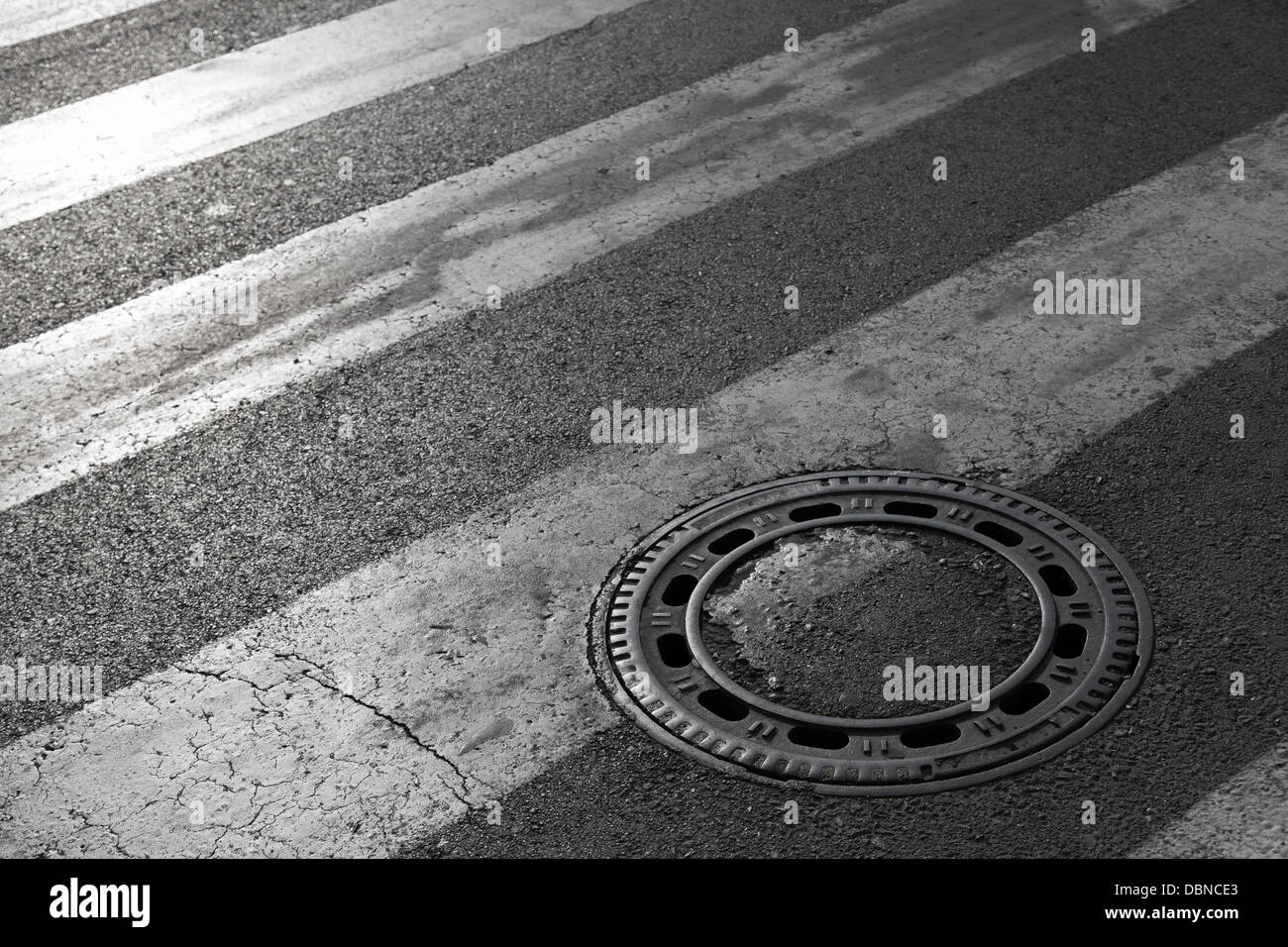 Sewer manhole cover on asphalt road with pedestrian crossing marking ...