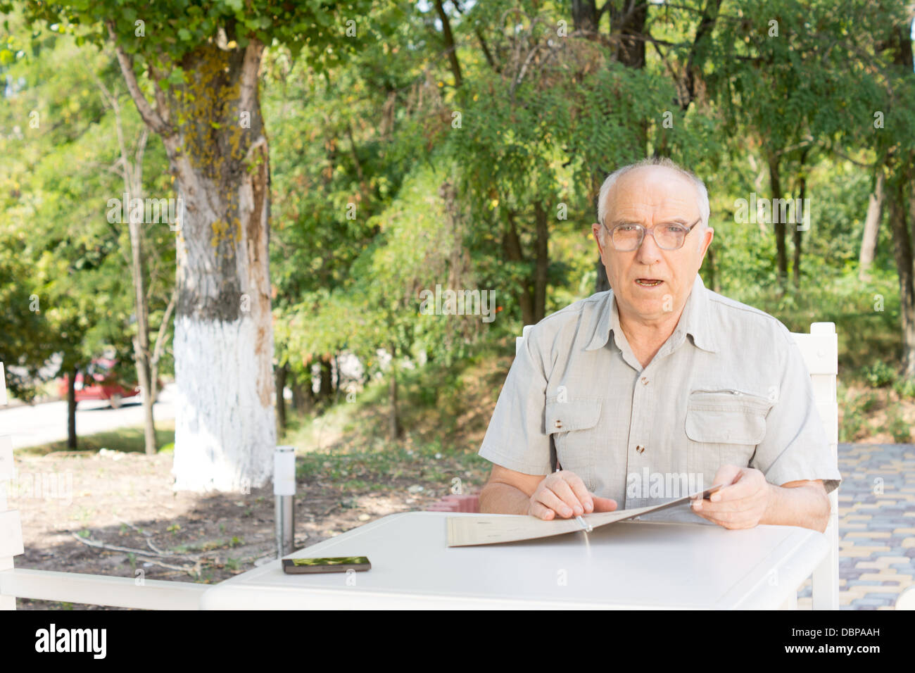 Senior man placing a food order sitting at an open-air restaurant with ...