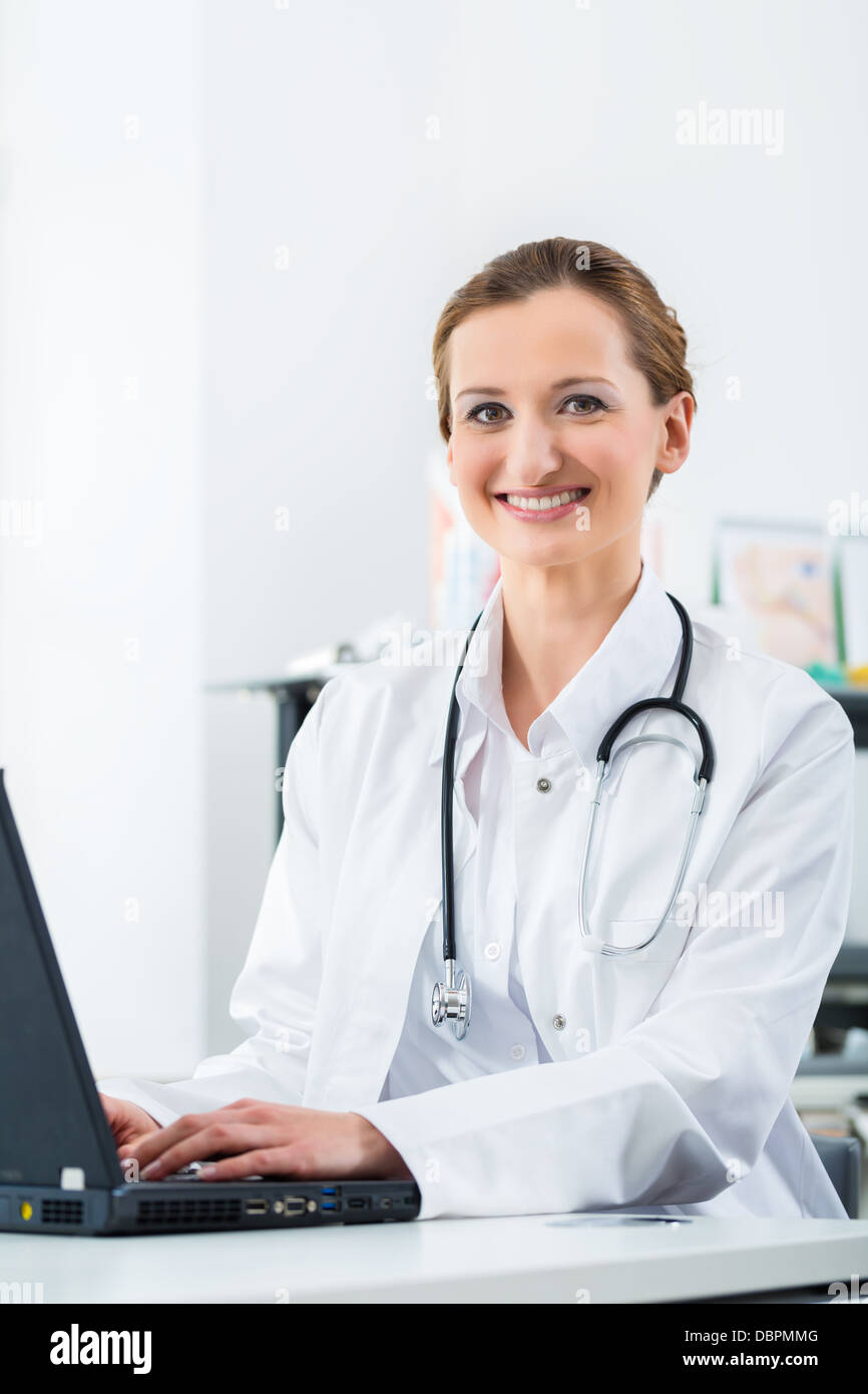 Young female doctor sitting at a desk in front of window in clinic ...