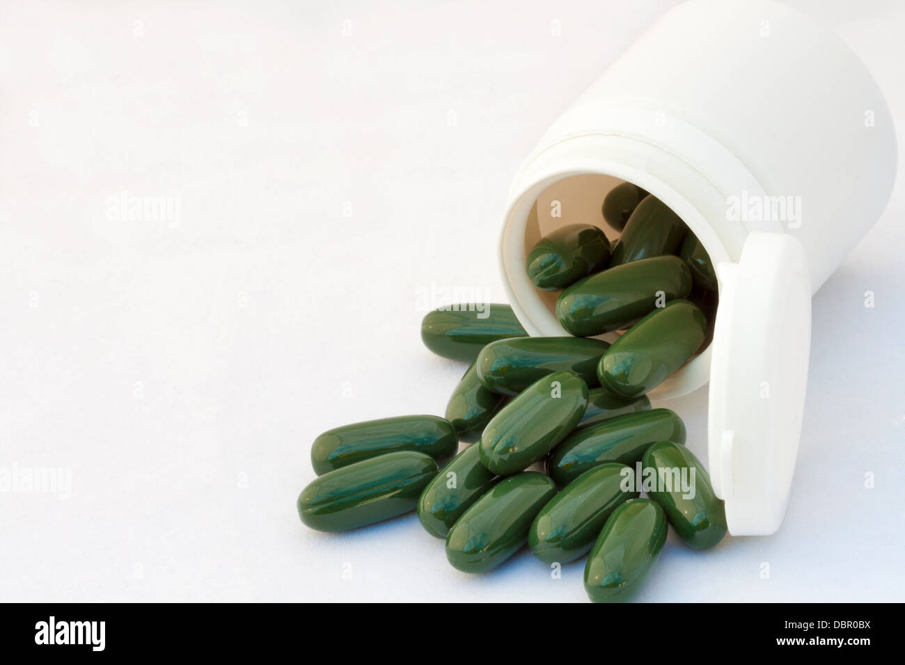 inverted bottle with green capsules closeup against white Stock Photo ...