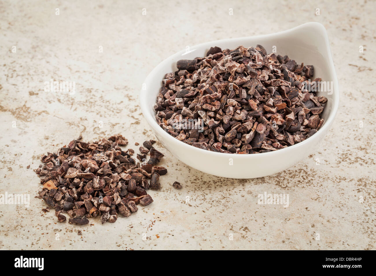 small ceramic bowl of raw cacao nibs against a ceramic tile background ...