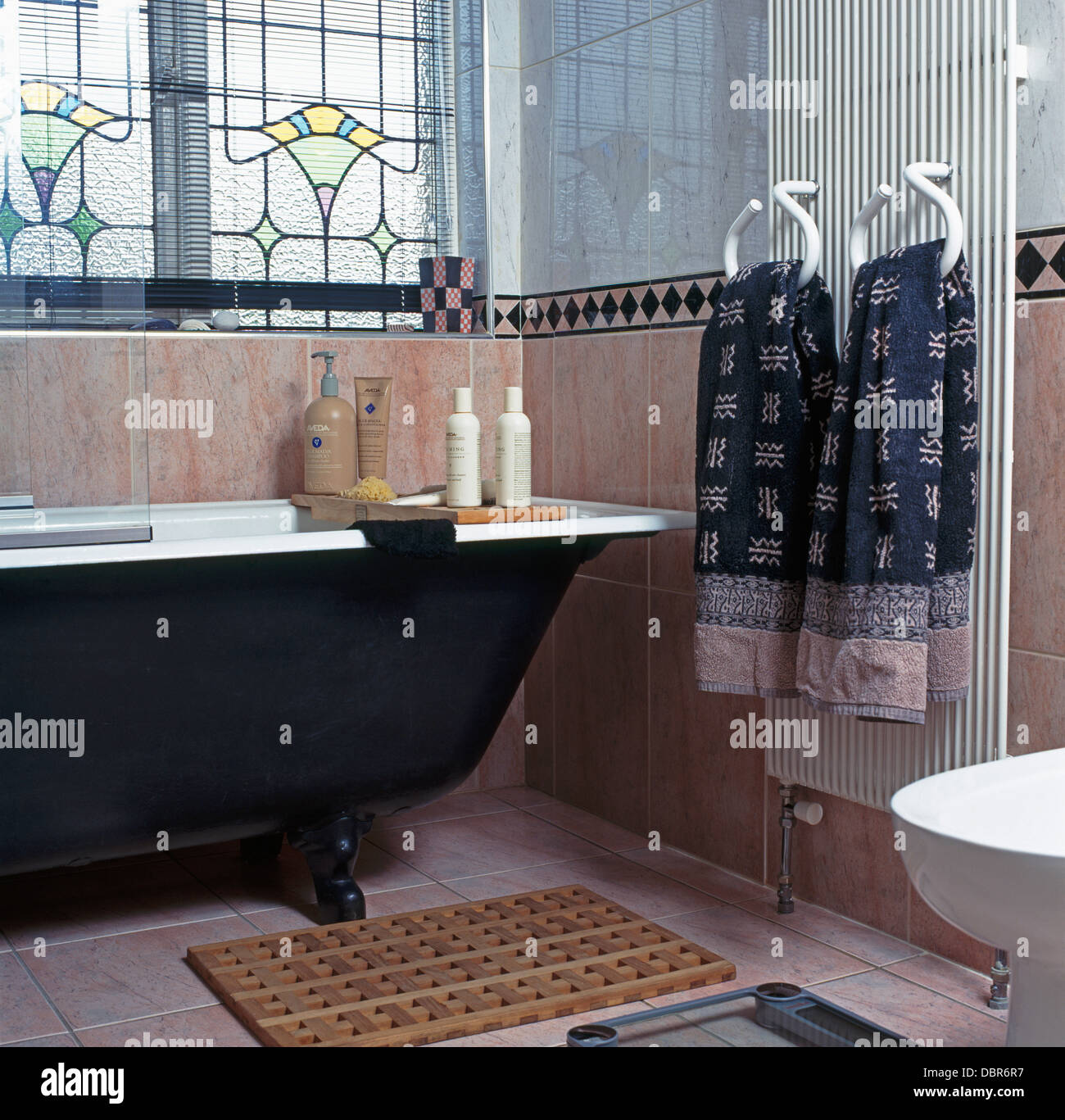 Black claw-foot bath below Edwardian-style stained glass window in ...