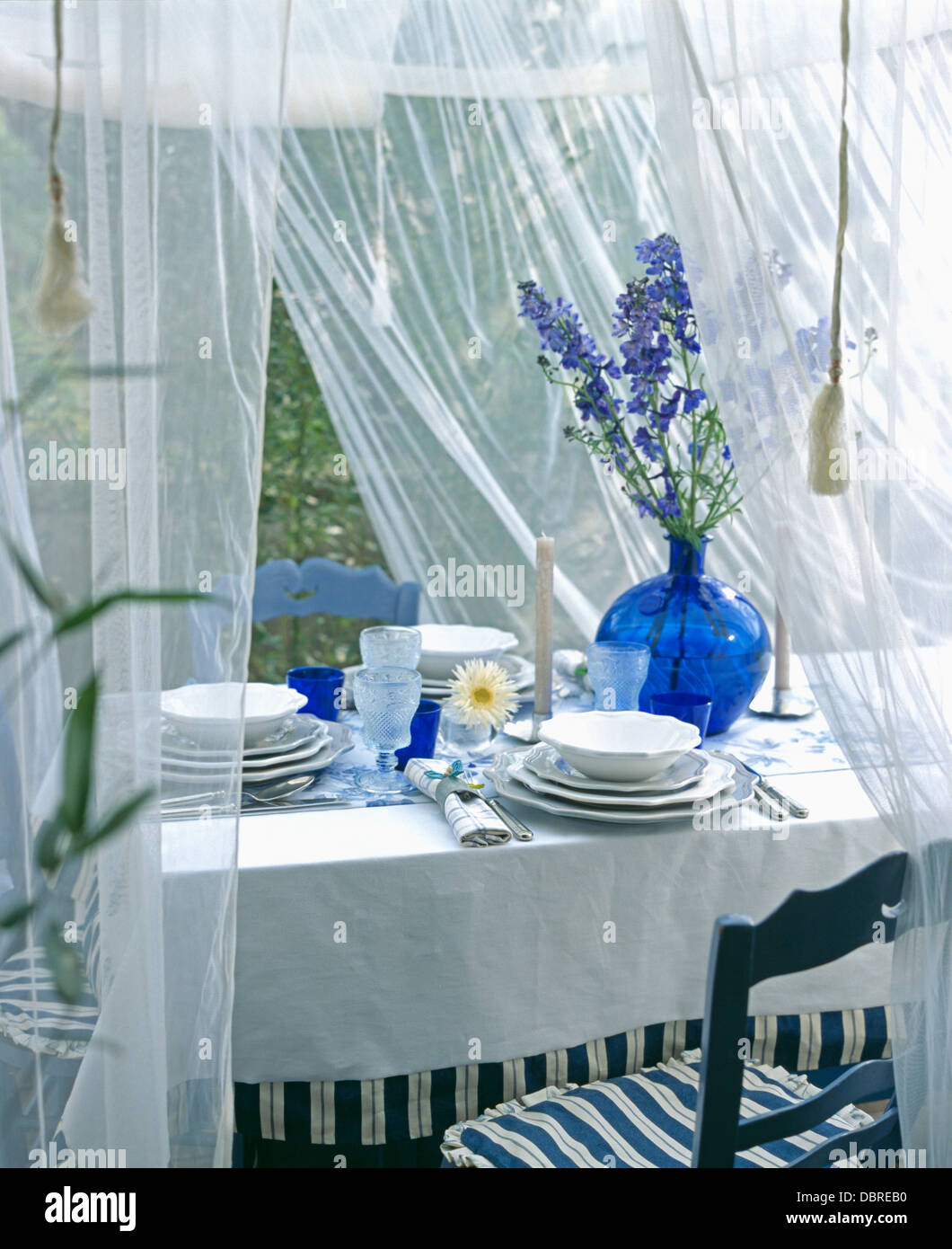 White voile drapes above garden table with set for lunch with white ...