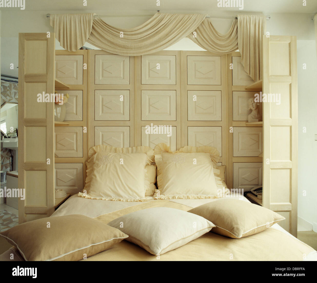 Draped fabric and panelled screen above bed with cream cushions in ...