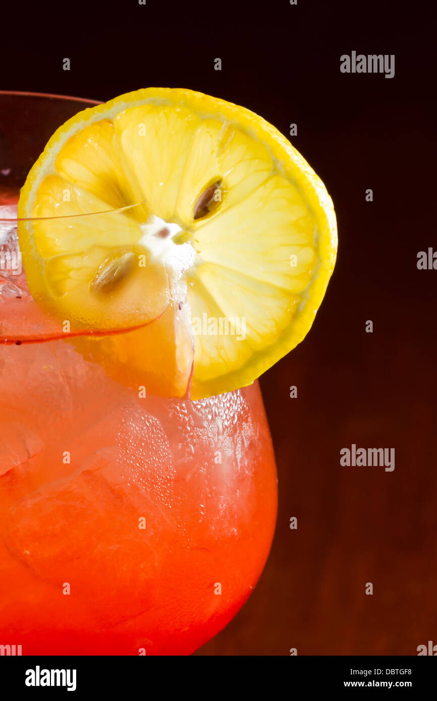 red cocktail isolated on a bar with a dark background garnished with a ...