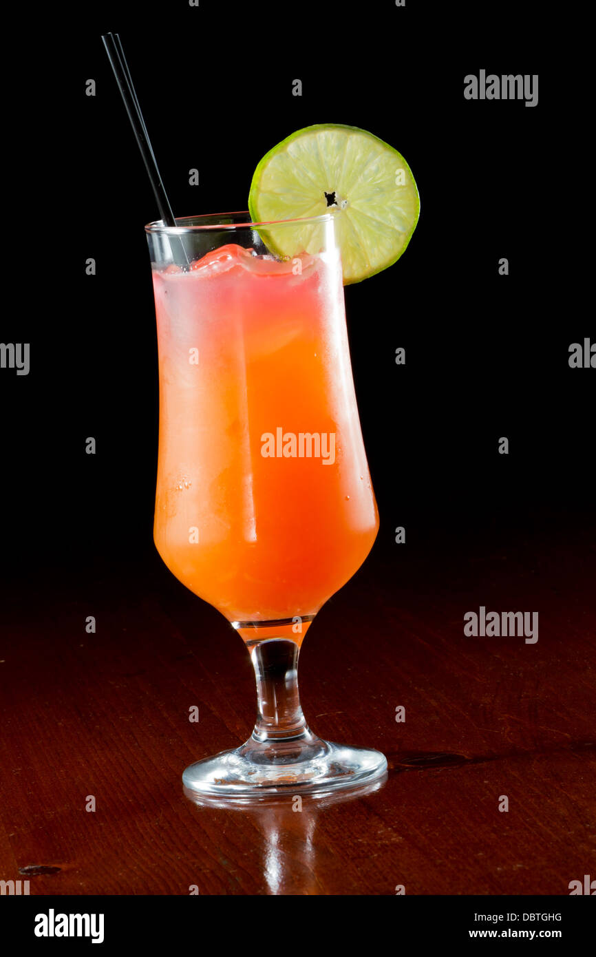 tropical juice cocktail served on a dark bar garnished with a lime ...