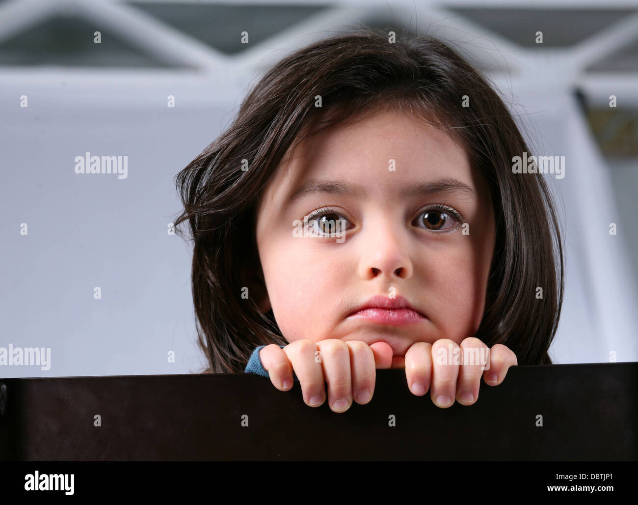 serious little brunette girl peeking over edge Stock Photo - Alamy